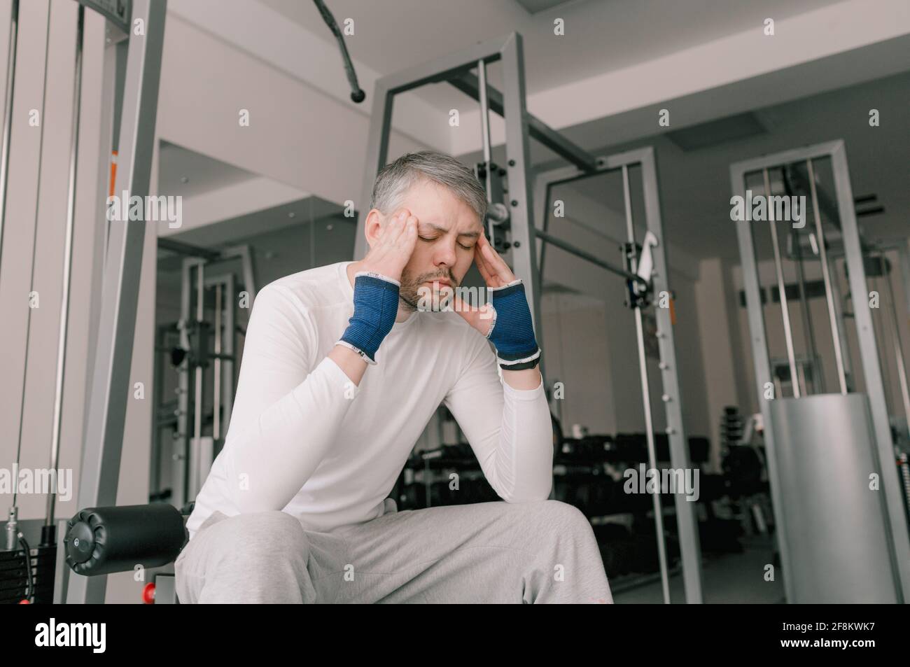 a tired athlete after a hard workout sits holding his head. headache ...