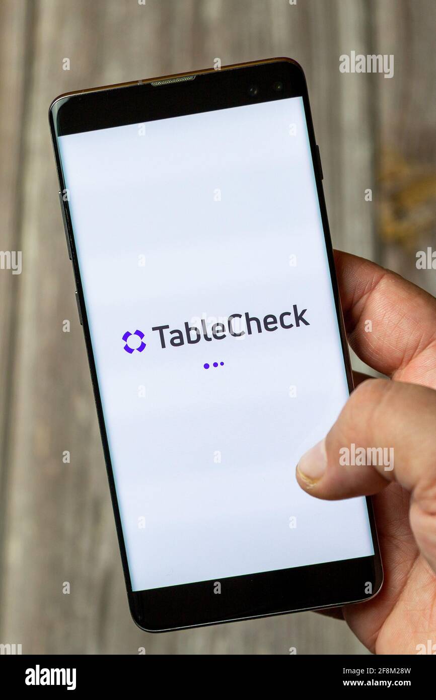 A Mobile phone or Cell phone being held in a hand showing the Tablecheck app on screen Stock ...
