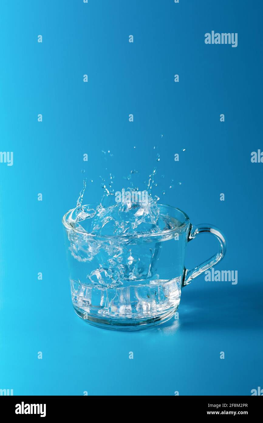 Clear cold water in a glass cup on a blue background. Splash from ...
