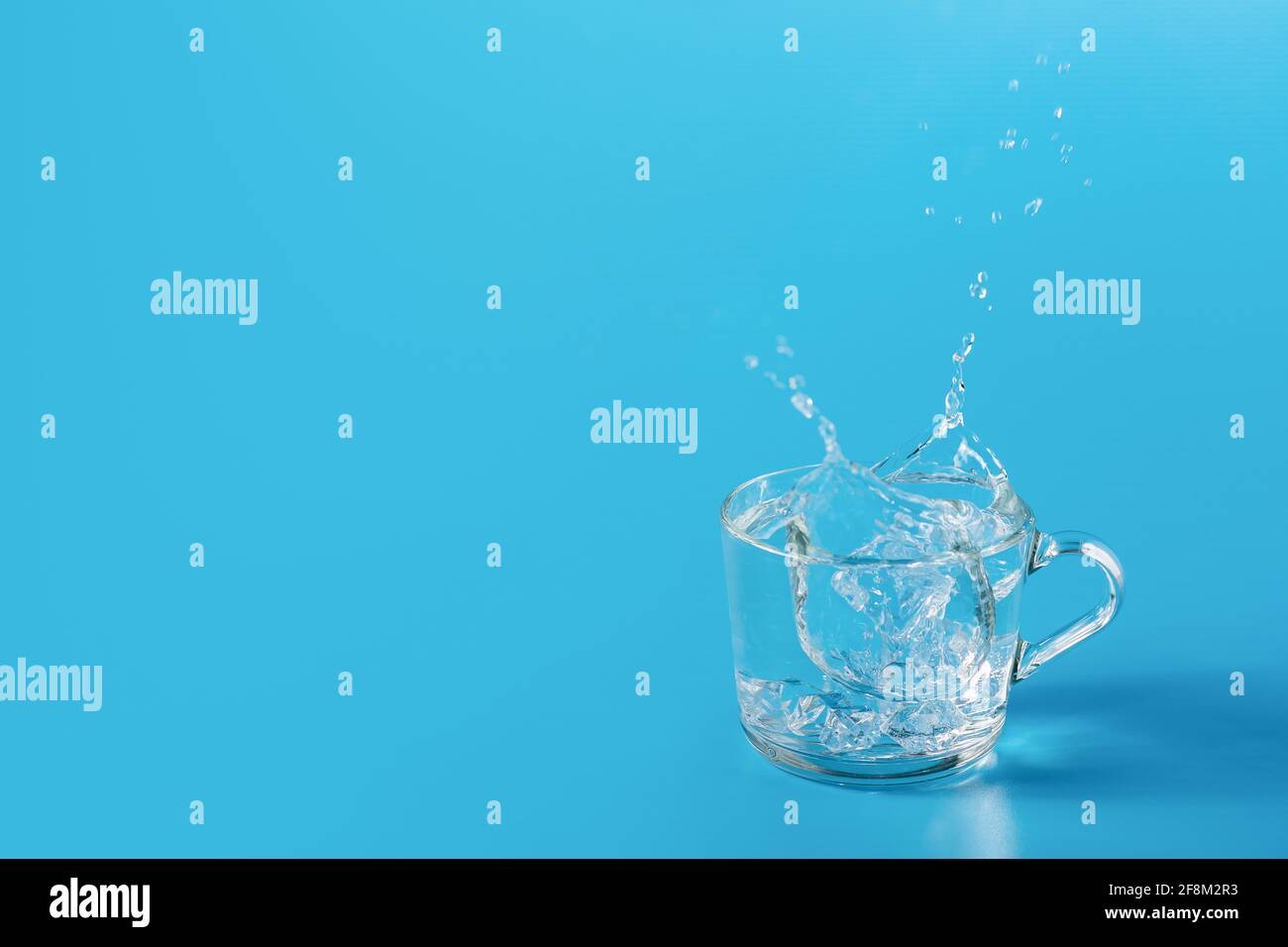 Clear cold water in a glass cup on a blue background. Beautiful splash ...