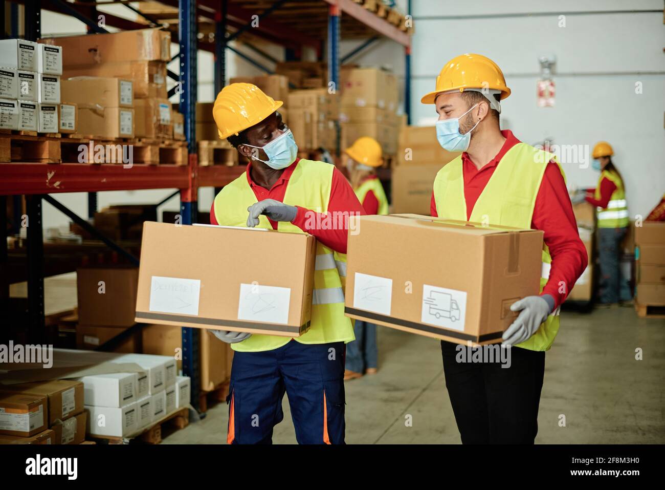 Multiracial warehouse workers holding delivery boxes while wearing ...