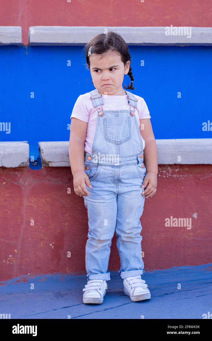 Little Caucasian girl, combed with braids and dressed in denim overalls ...