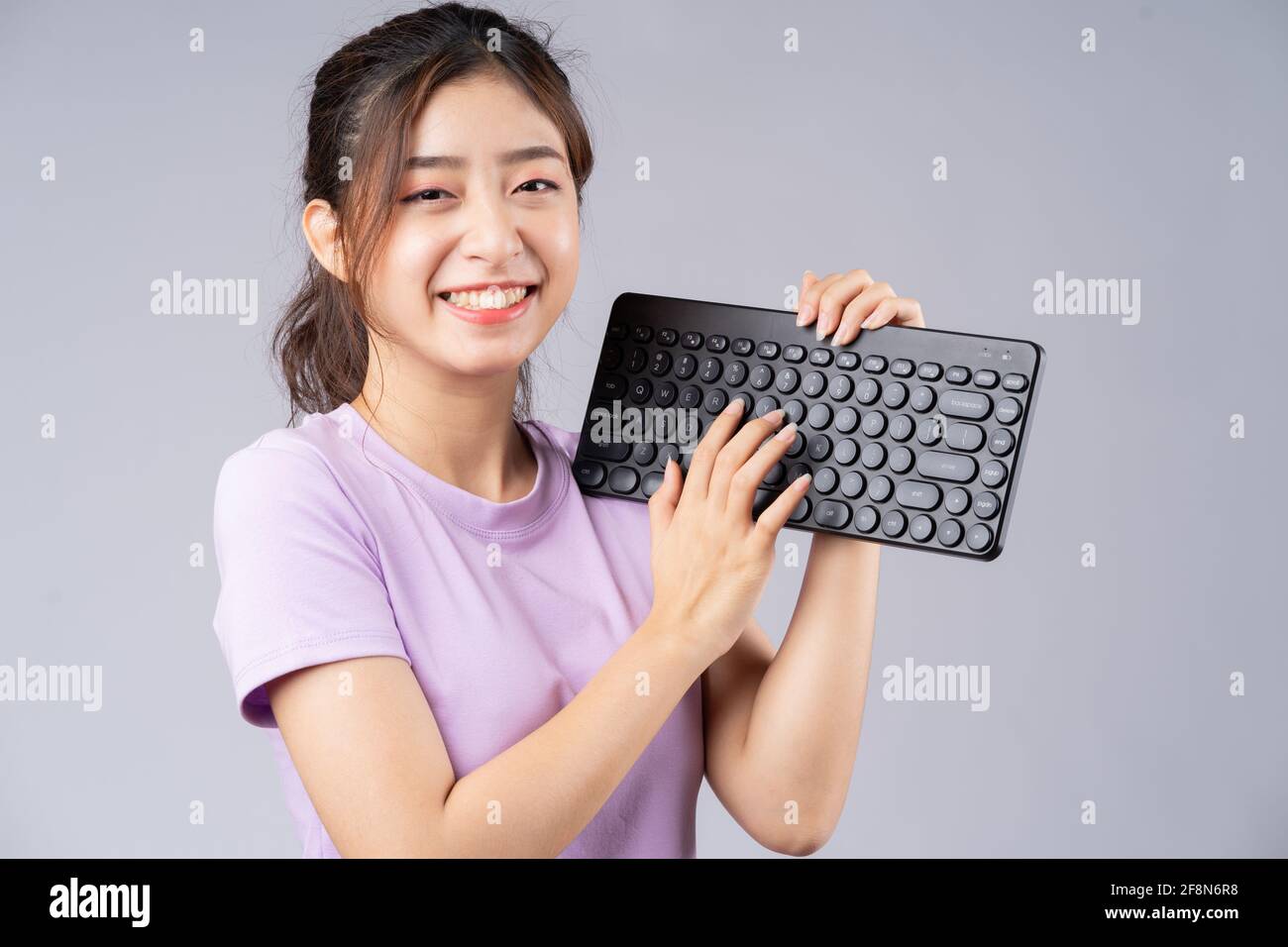Young Asian girl using keyboard on grey background Stock Photo - Alamy