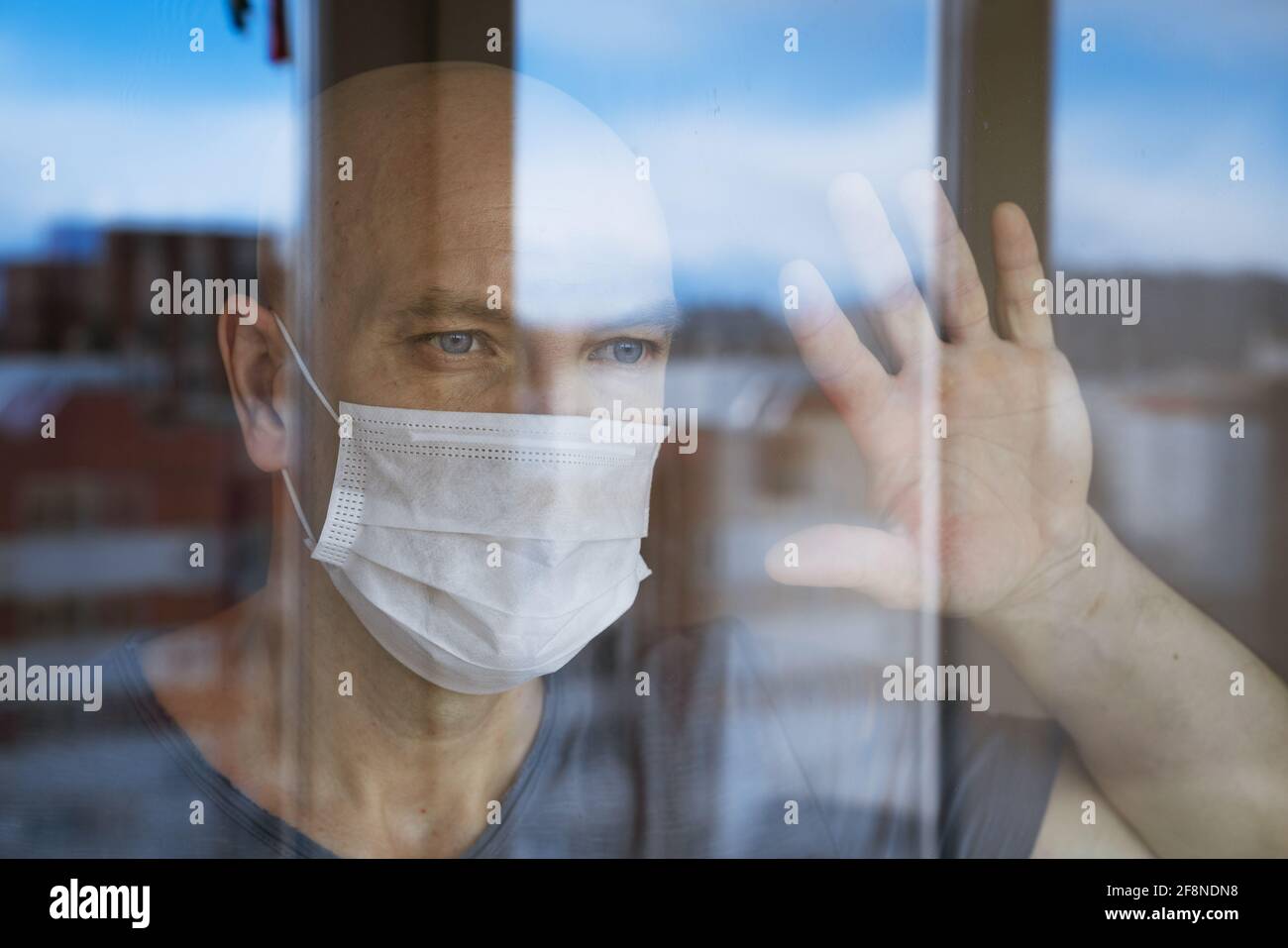 portrait of a bald man in a protective mask looking through the windows ...