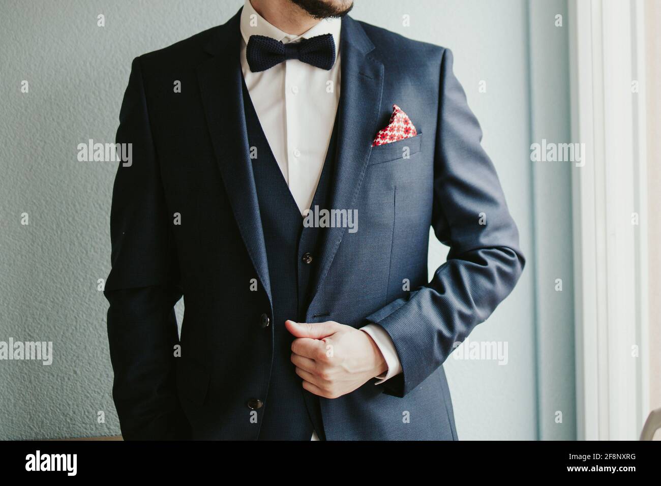 Man dressed in classy suit with bowtie posing in front of bright wall ...