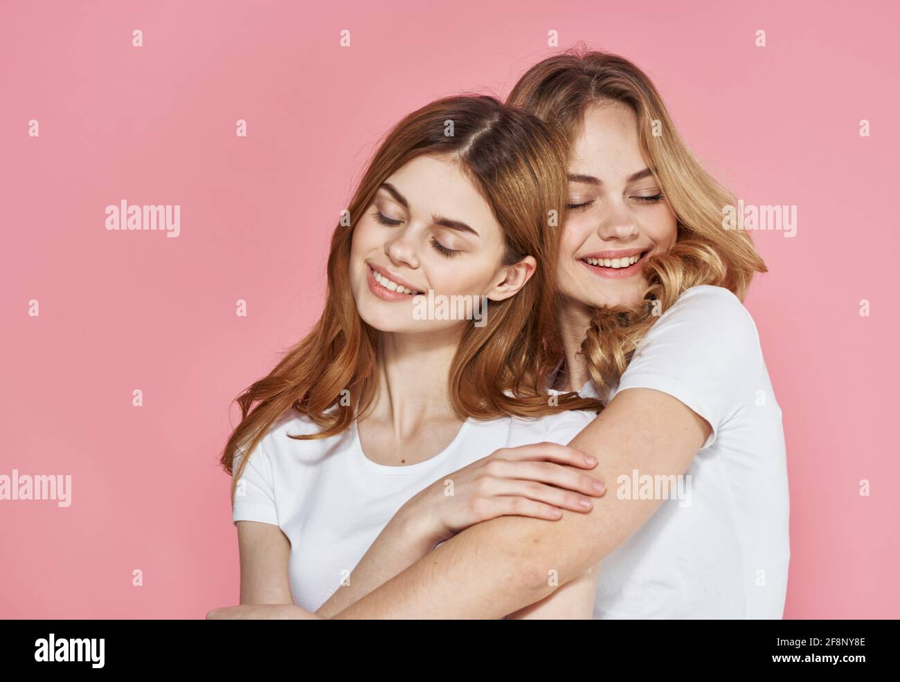 Two glamorous girlfriends hugs caring emotions fun pink background ...