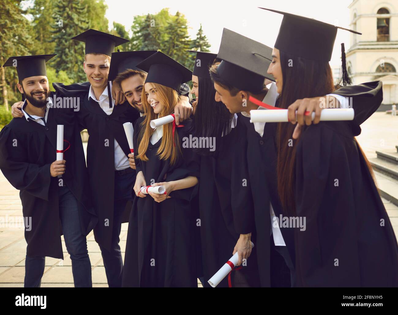 Group of smiling university graduates standing with diplomas, hugging ...