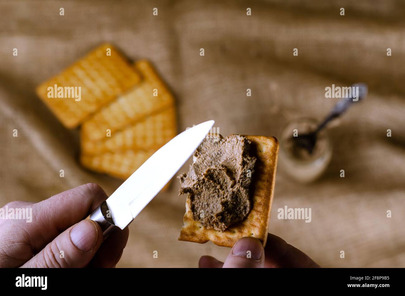 Close-up of a hand spreading pate on a cracker with a knife. A man ...