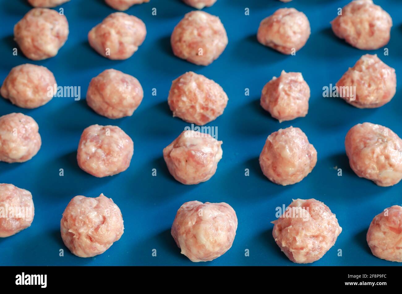 Raw shaped meatballs on blue. Rows of meatballs with pepper, salt and ...