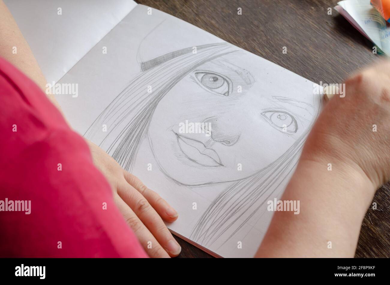 An adult woman draws a portrait with a pencil on paper. The process of ...