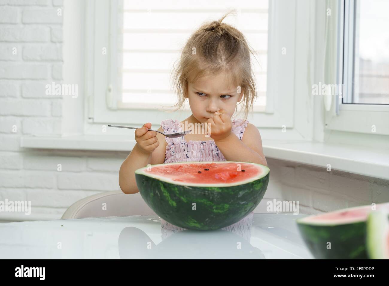 angry hungry little girl eating half a watermelon with a spoon and ...