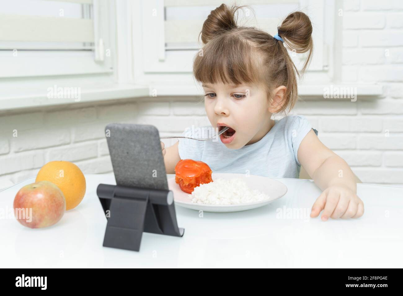 kid girl eating food and watching cartoons on a smartphone Stock Photo ...