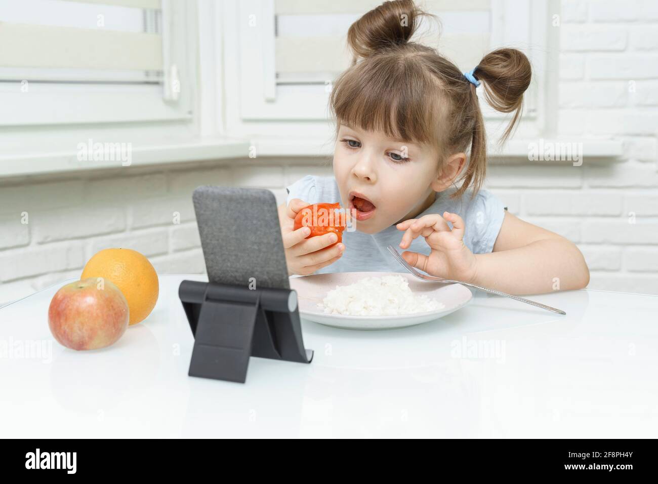 kid girl eating food and watching cartoons on a smartphone Stock Photo ...