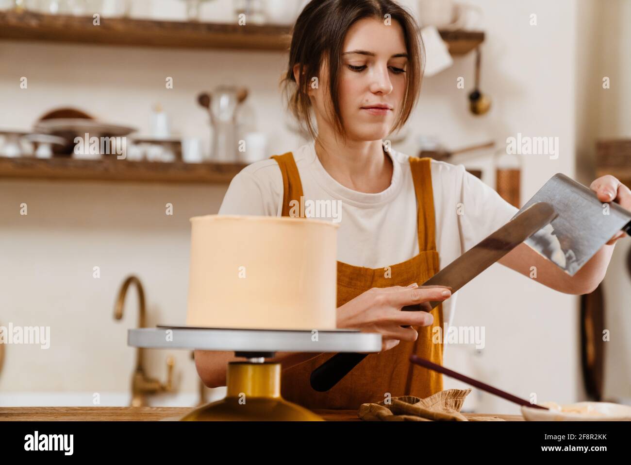 Beautiful concentrated pastry chef woman making cake with cream at cozy ...