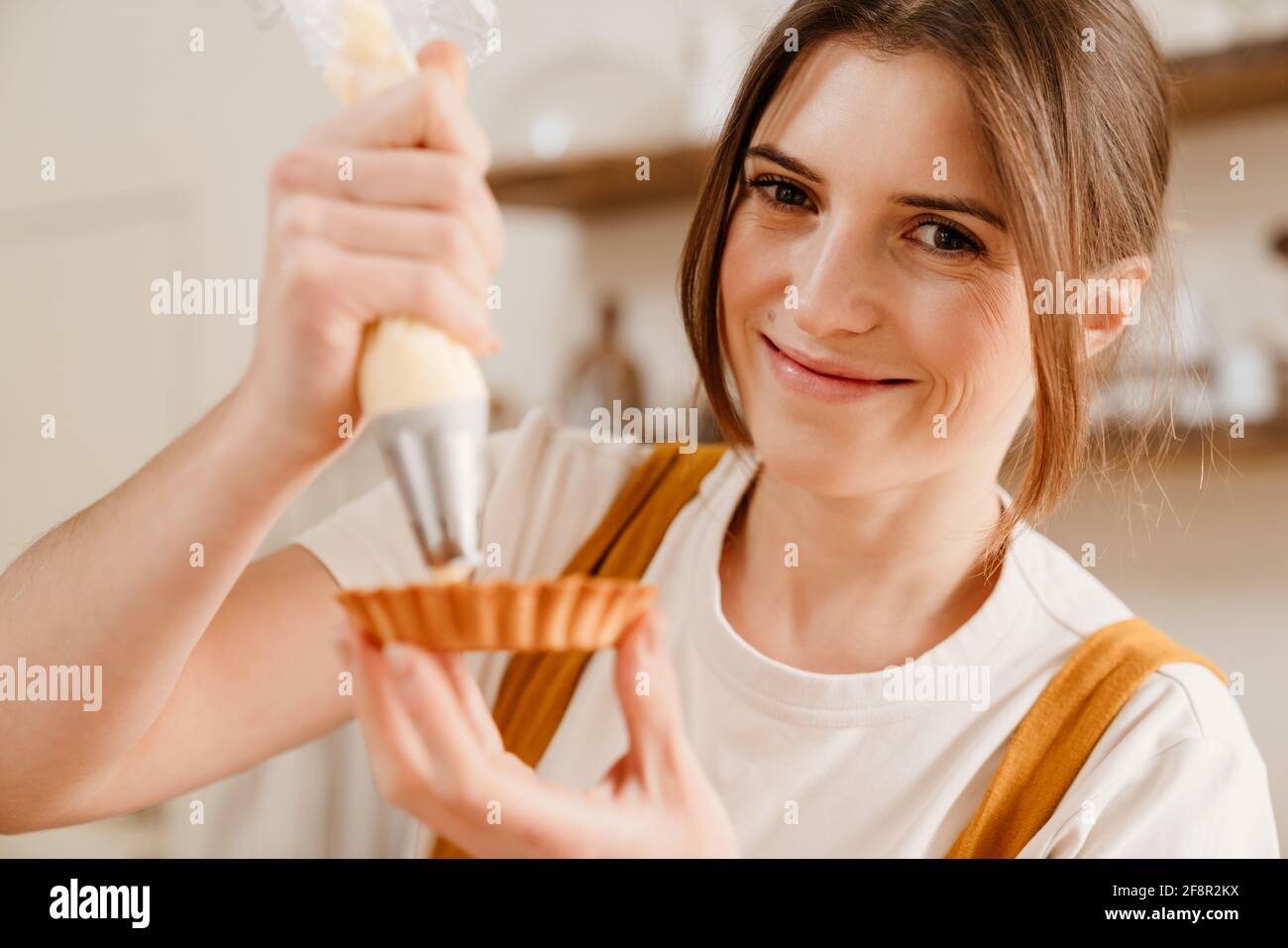 Beautiful happy pastry chef woman smiling while making tart with cream ...