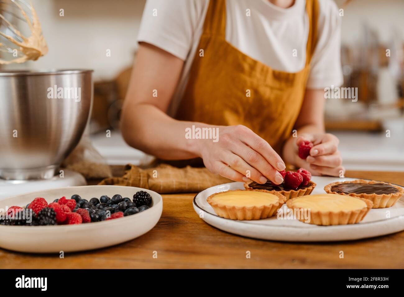 Caucasian pastry chef woman making tarts with berries at cozy kitchen ...