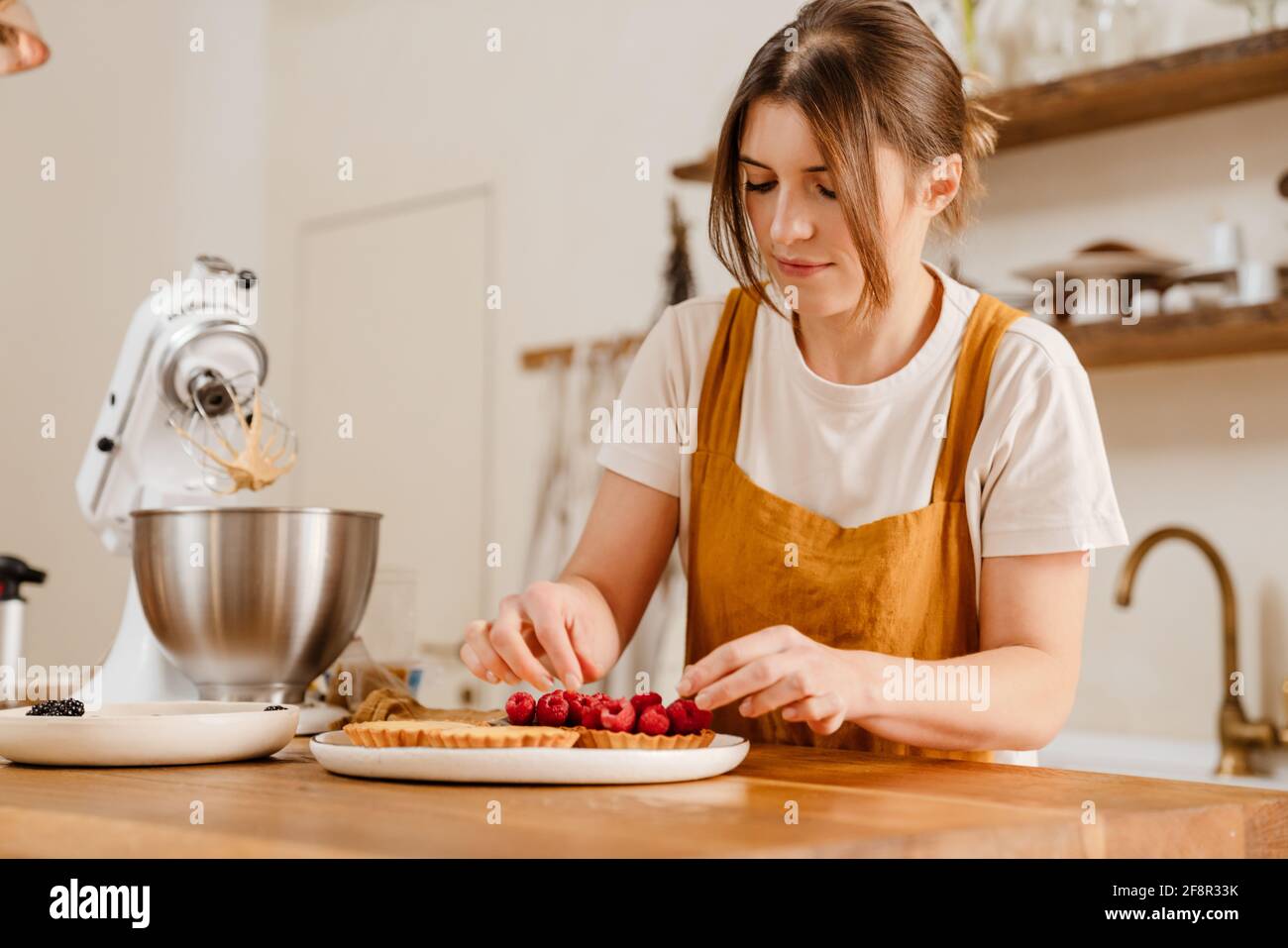 Beautiful concentrated pastry chef woman making tarts with berries at ...