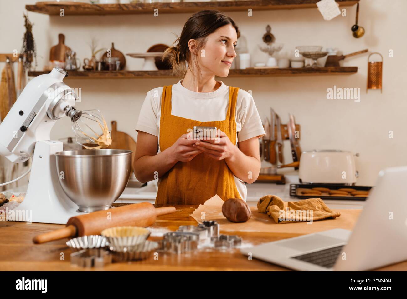 Smiling pastry chef woman using mobile phone while cooking cake at cozy ...