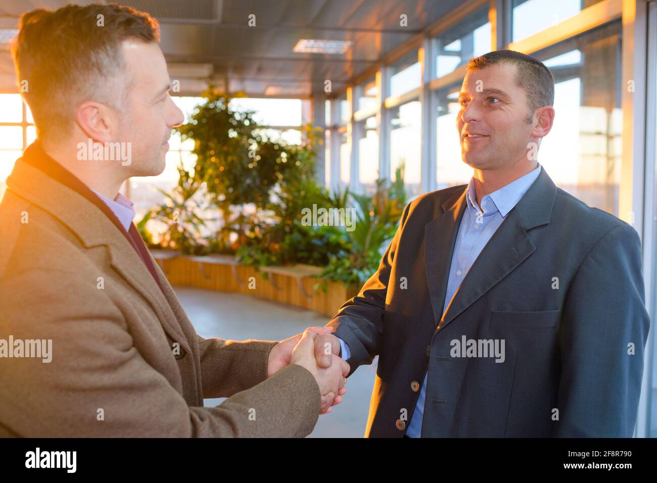 two businessmen shaking hands in lobby of modern office Stock Photo - Alamy