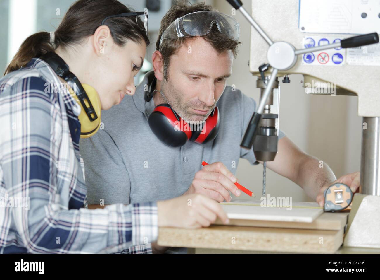 worker showing female apprentice how to use bench drill Stock Photo - Alamy