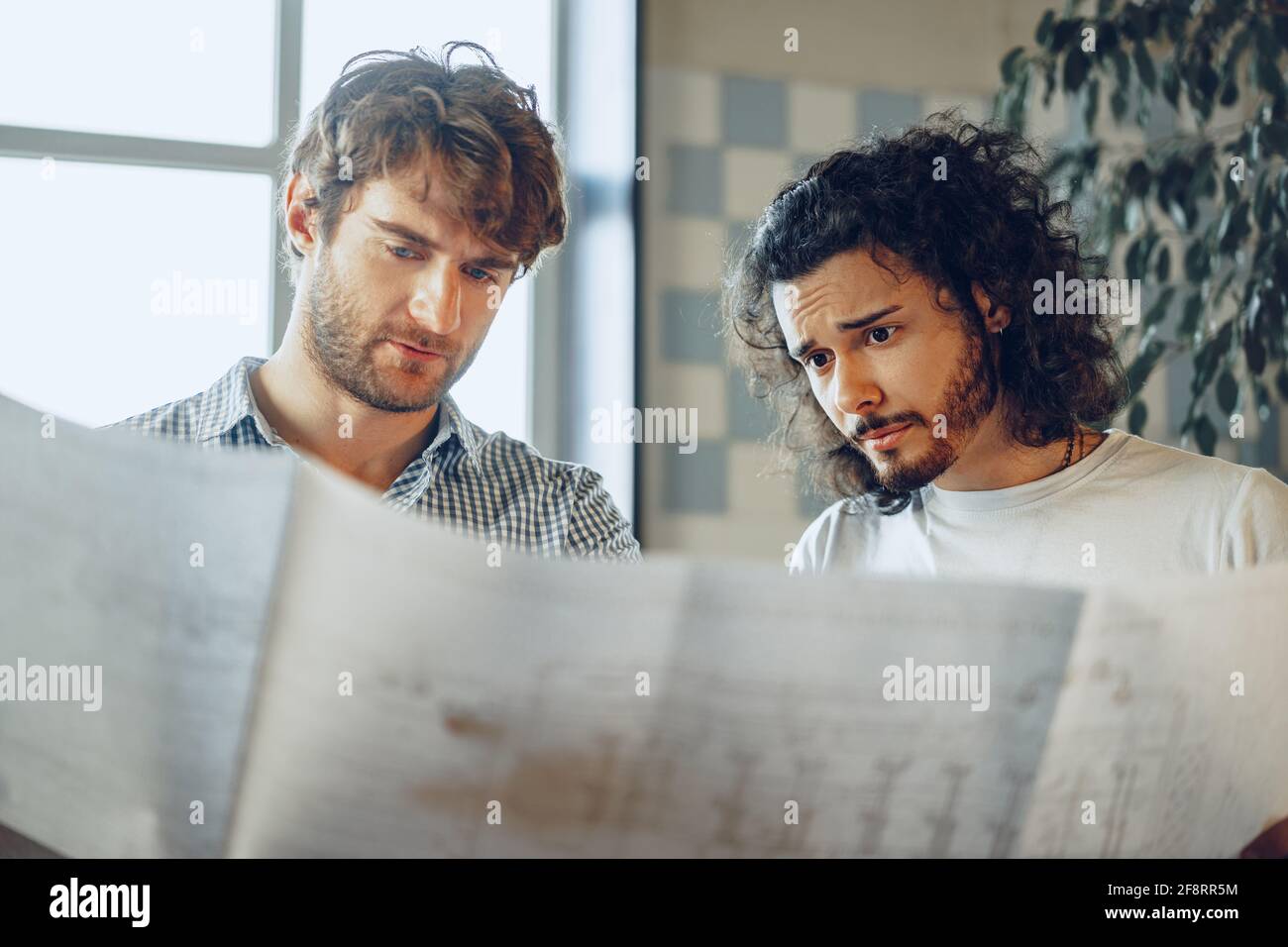 Two young businessmen looking at blueprint and discussing it Stock ...