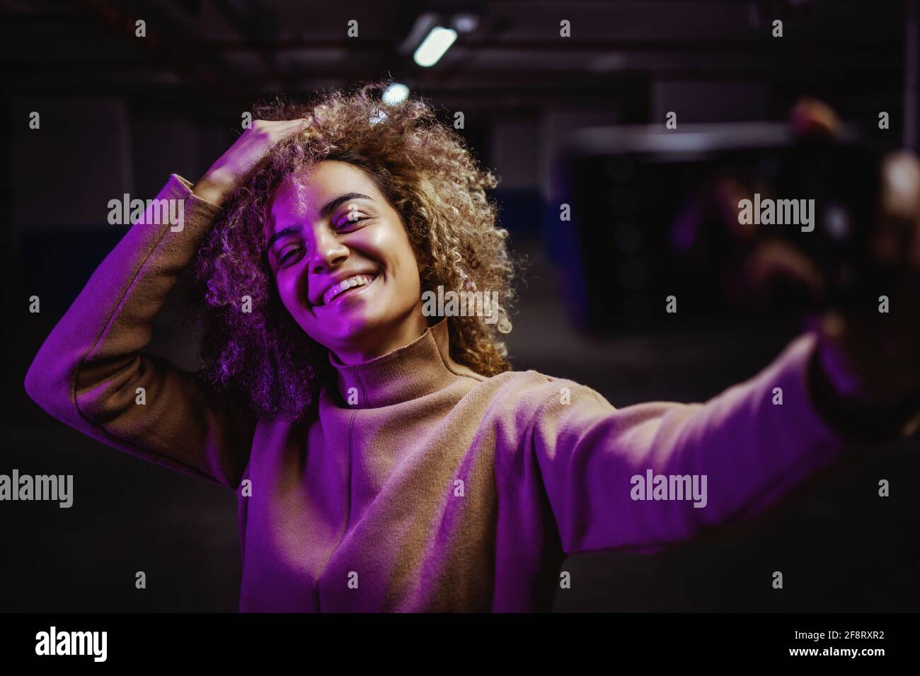 Smiling mixed race trap girl standing in underground garage and taking ...