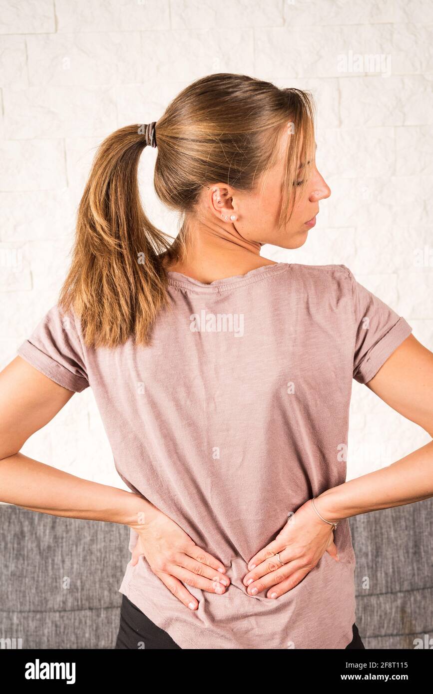 Lower back pain; blonde European woman holding hands on her back Stock ...