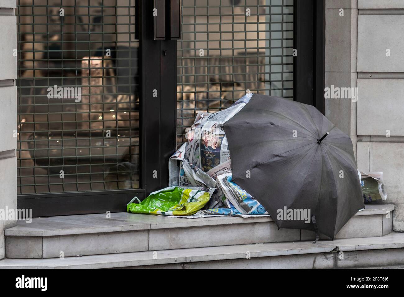 A homeless person sleeps under and umbrella and newspapers on the steps ...