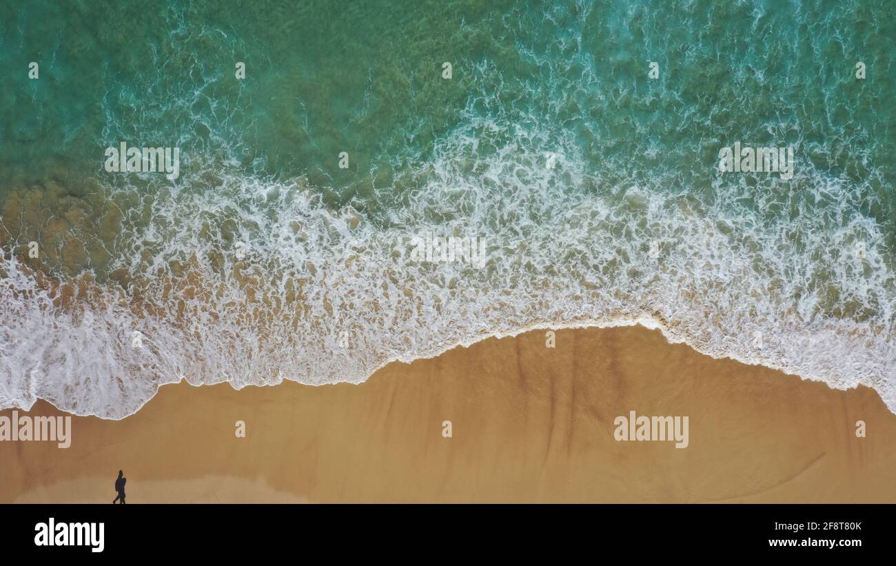 Aerial view of the wavy ocean hitting the sandy beach on the coast ...