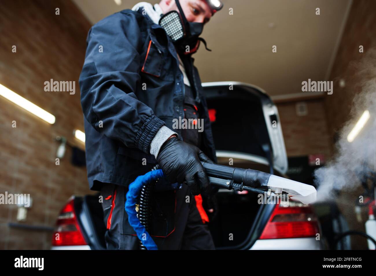 Man in uniform and respirator, worker of car wash center, cleaning car ...
