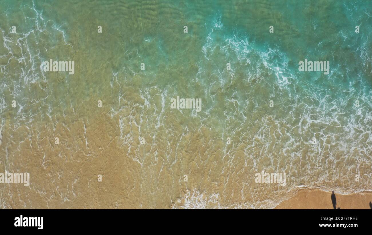 Aerial view of the wavy ocean hitting the sandy beach on the coast ...