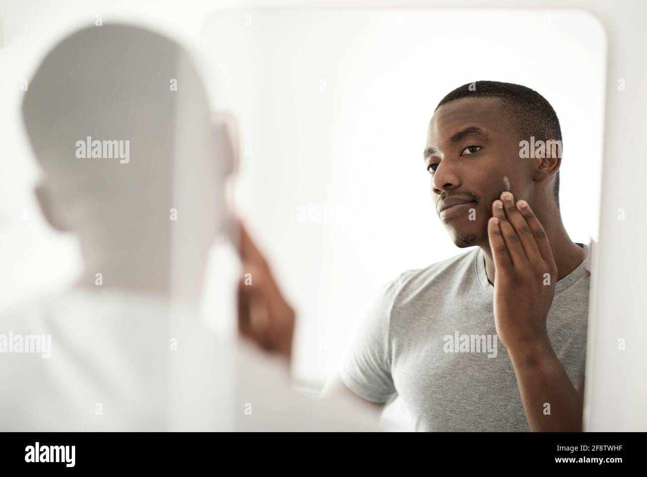 African man applying lotion on his face in his bathroom mirror Stock ...