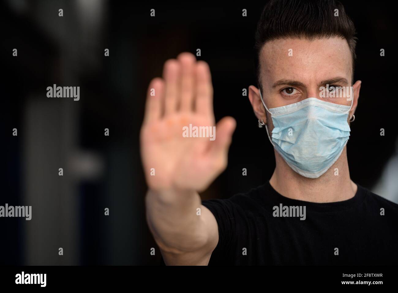 Portrait of young handsome man showing STOP gesture while wearing face ...
