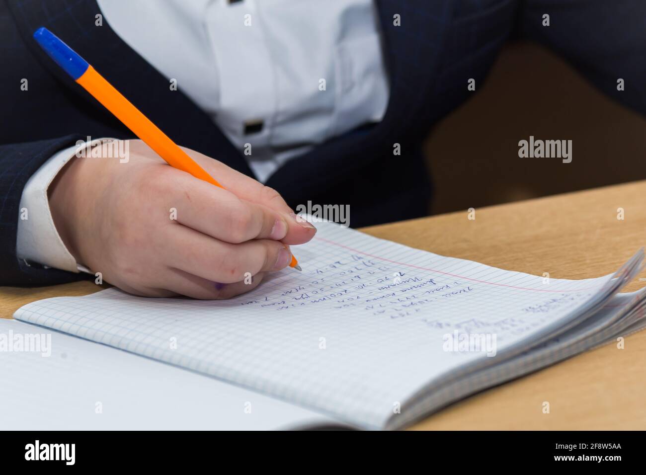 The boys hand with a fountain pen with blue ink solves math examples ...