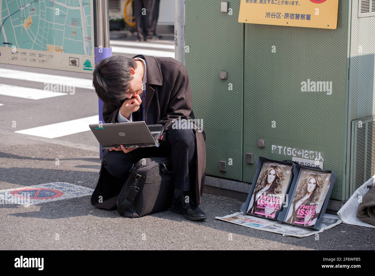 Japanese salaryman crouching on street with his laptop beside copies of ...