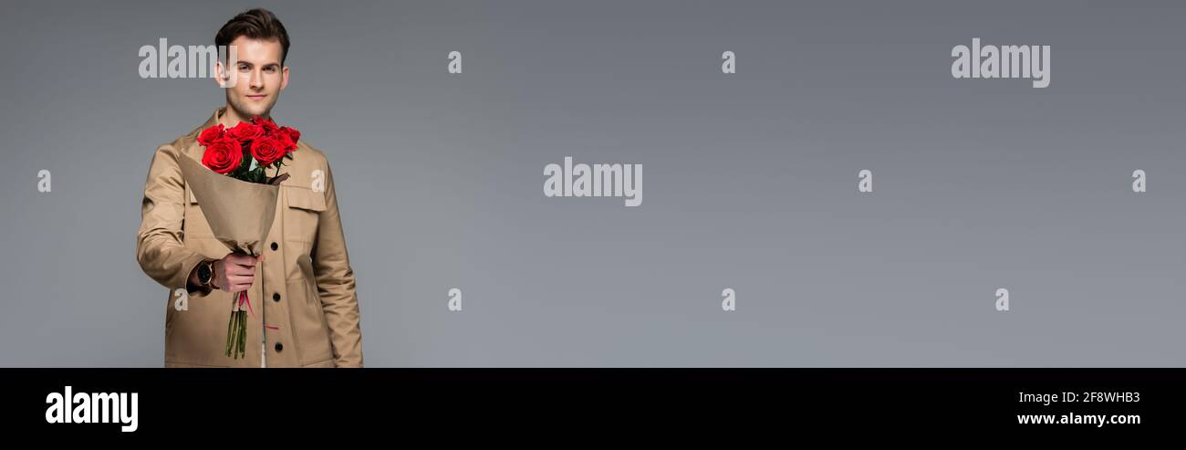 trendy man holding bouquet of red roses wrapped in paper isolated on ...