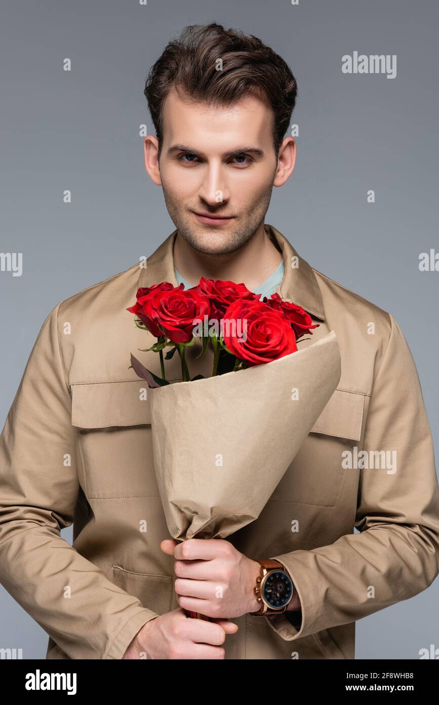 stylish man holding bouquet of red roses wrapped in paper isolated on ...