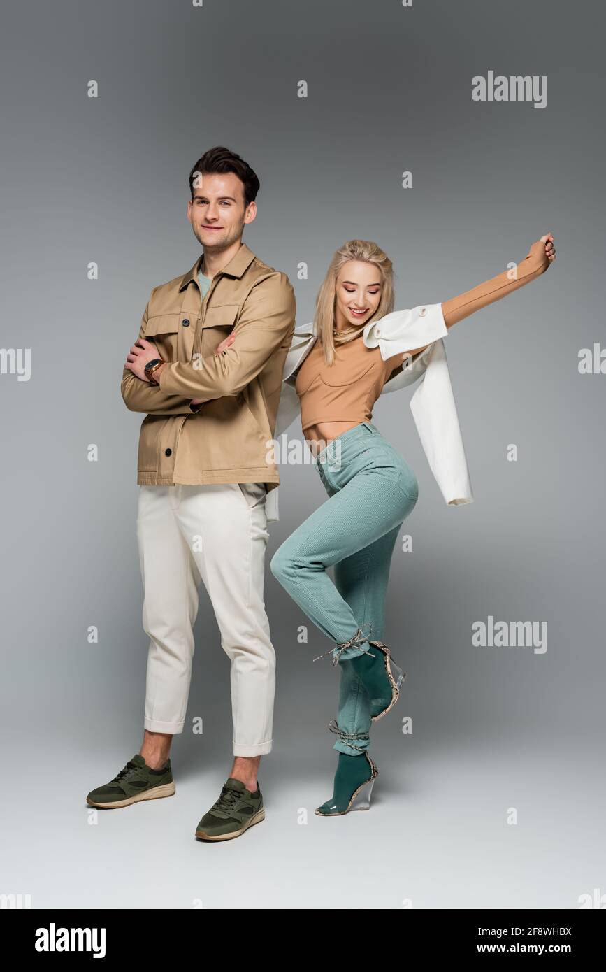 full length of stylish models in pants and jackets posing and smiling ...