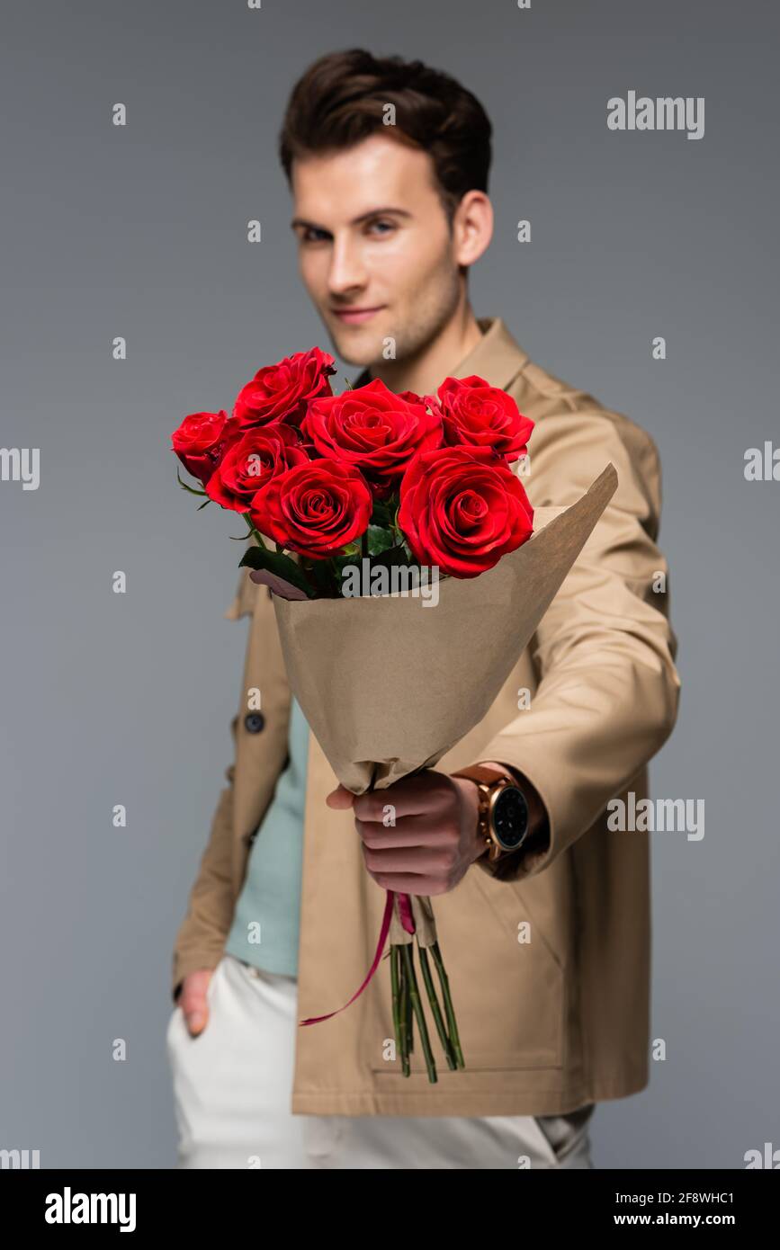 blurred trendy man holding bouquet of red roses wrapped in paper ...