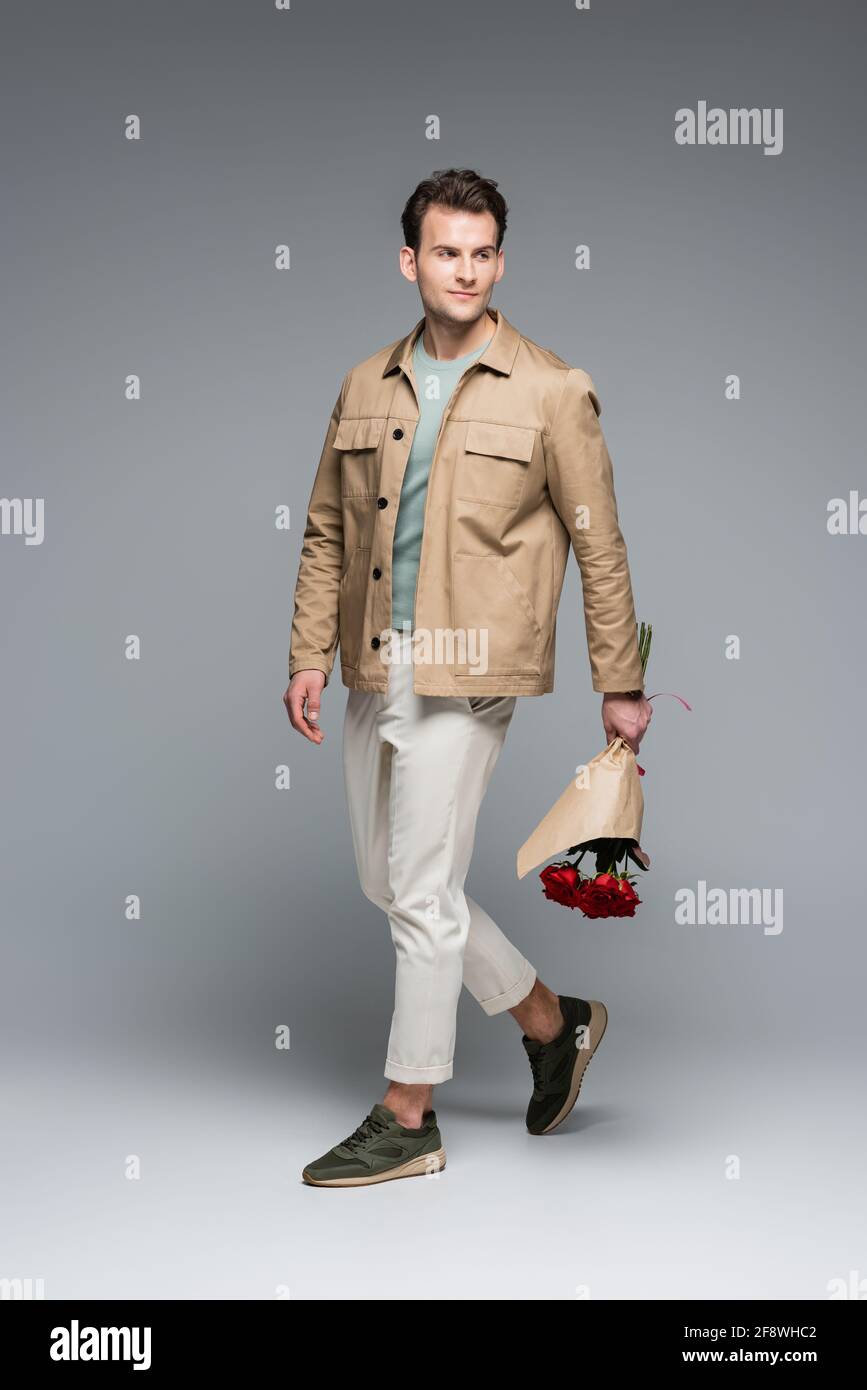 full length of trendy man holding bouquet of red roses wrapped in paper ...