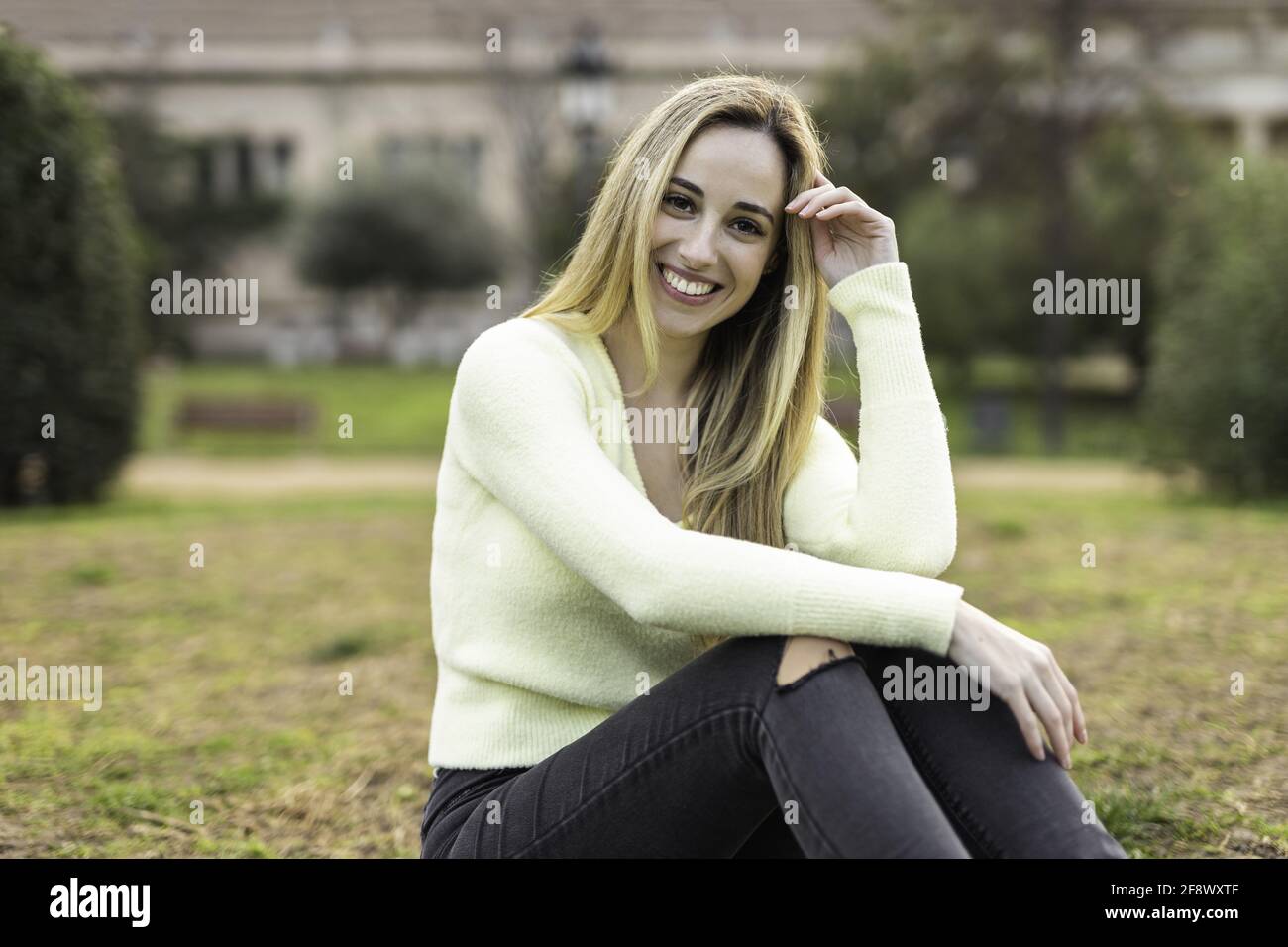 Shallow focus of a smiling Spanish woman sitting on grass outdoors ...