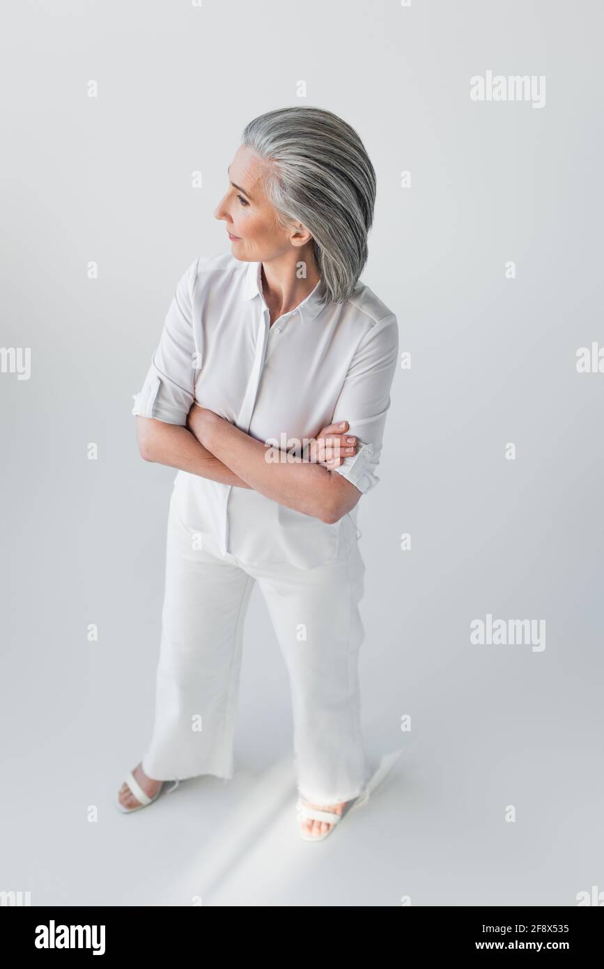 Overhead view of mature woman standing with crossed arms on grey ...