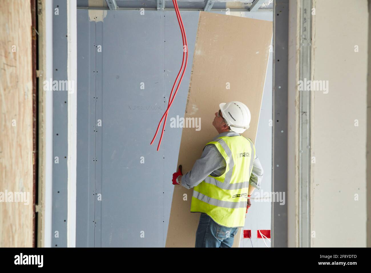 Construction worker on building site carries sheet of plaster board ...