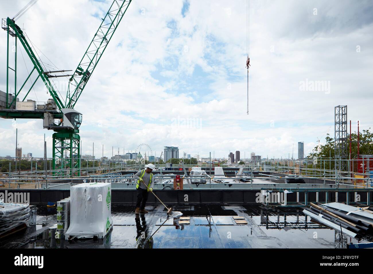 Construction worker sweeps rain from roof of building site with views ...