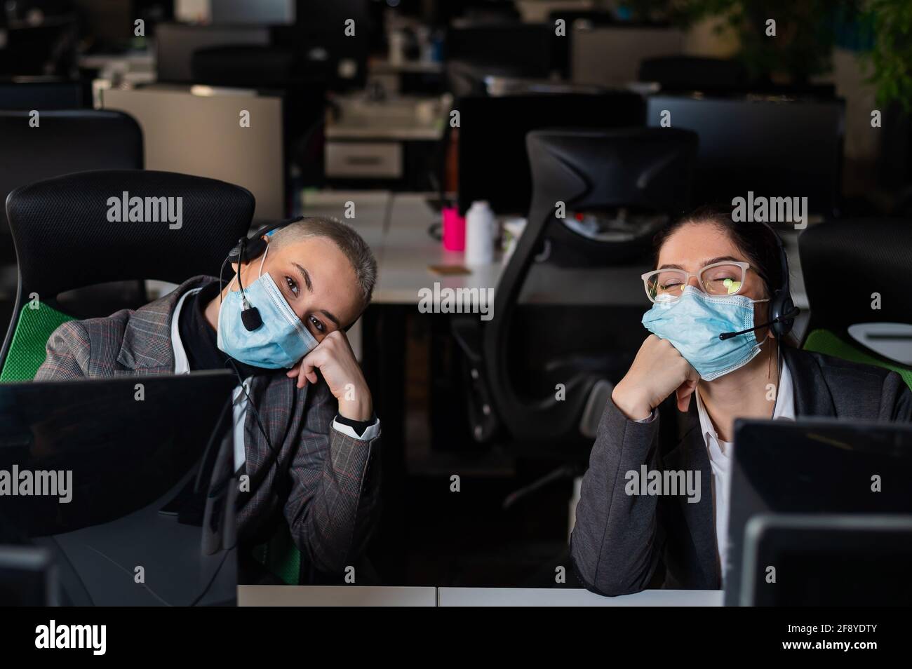 Two women in protective masks are bored at work. Call center operators ...