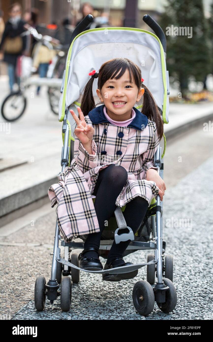 Cute young wealthy Japanese child gives peace sign sitting in younger ...