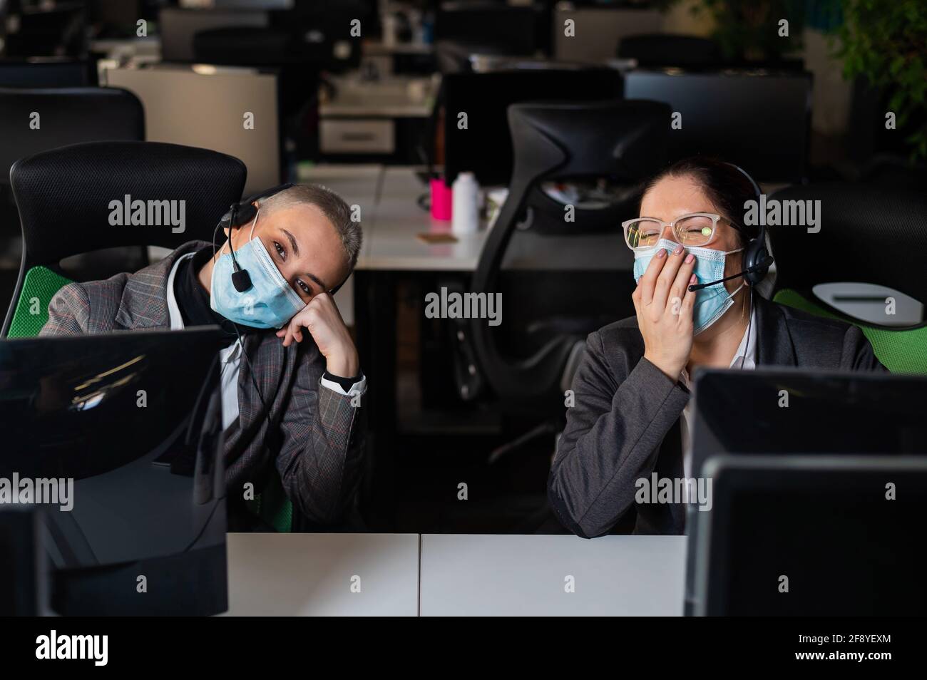 Two women in protective masks are bored at work. Call center operators ...