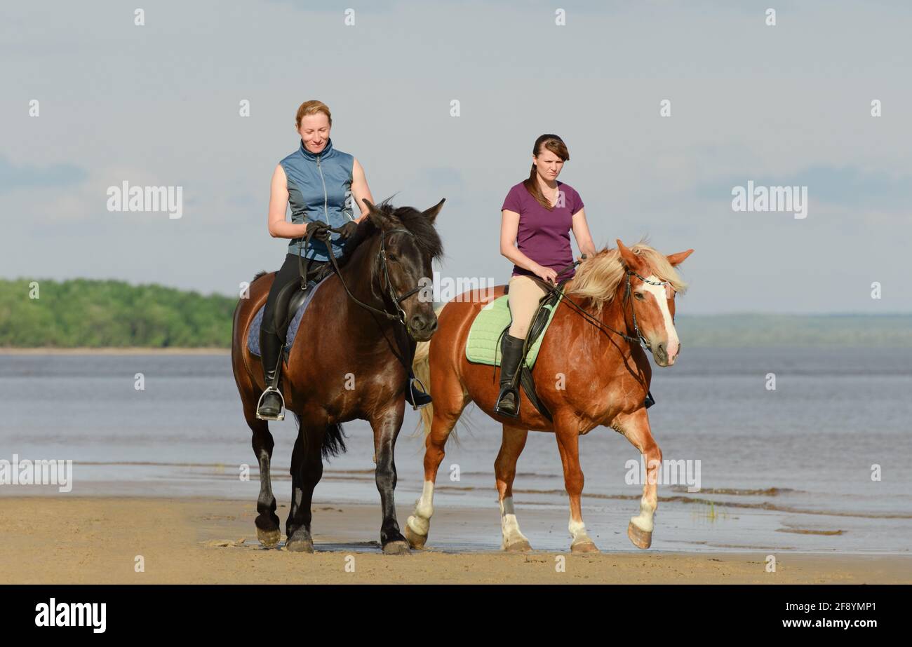 Two Caucasian women are riding on horseback on beach near a water Stock ...