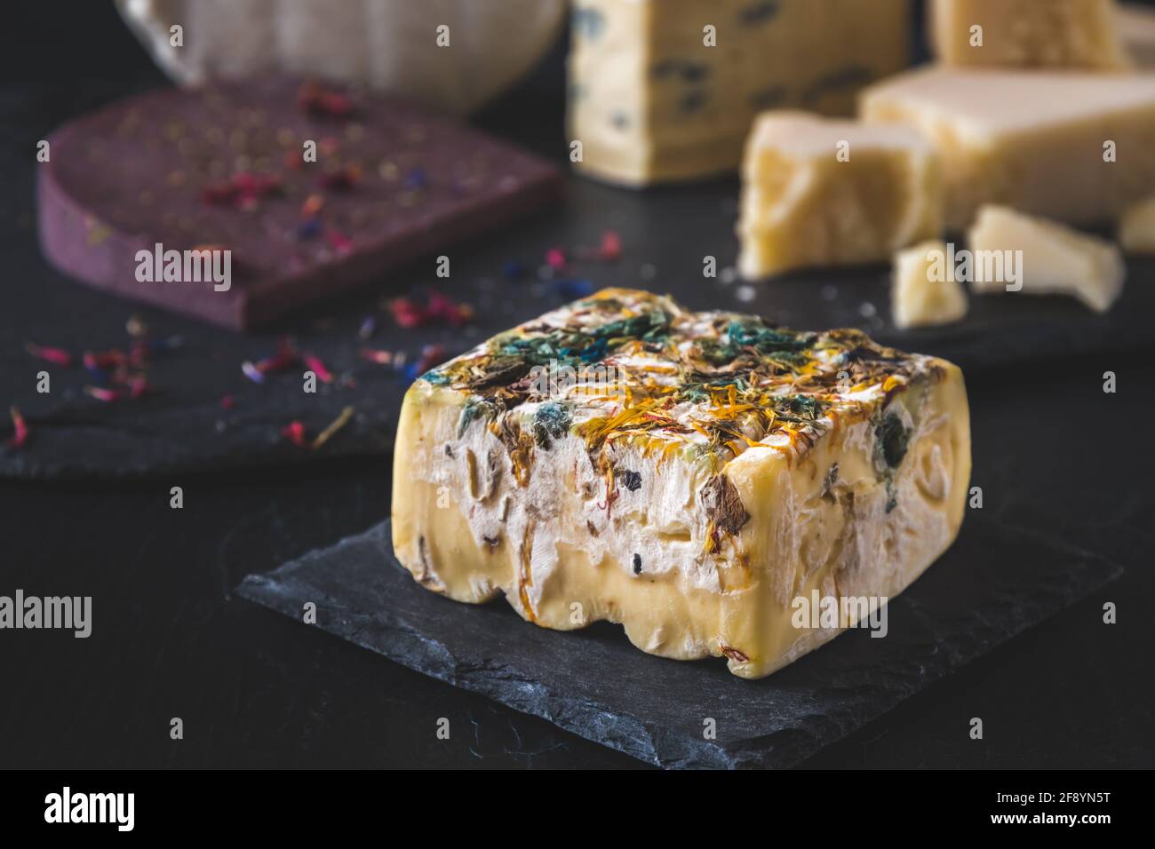 Square piece of soft cheese with colored edible flower petals on a ...