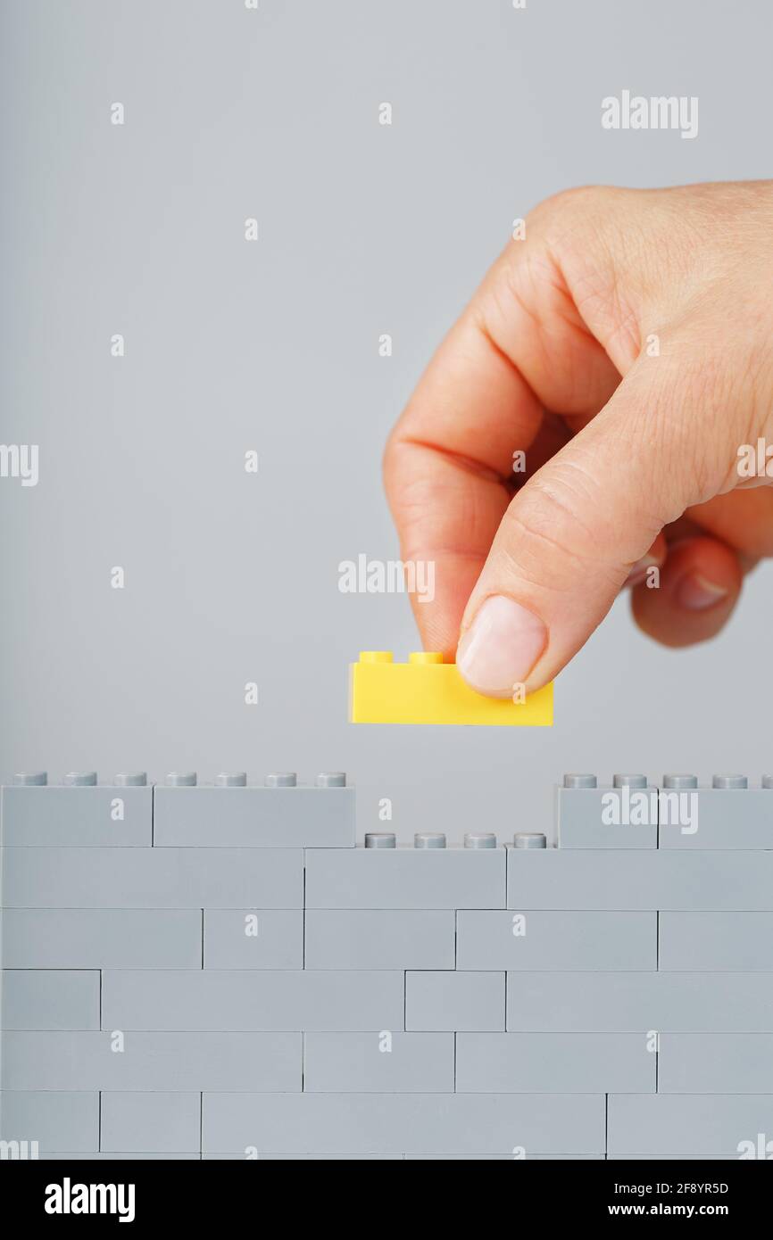The hand puts the last yellow brick on the gray wall from the ...